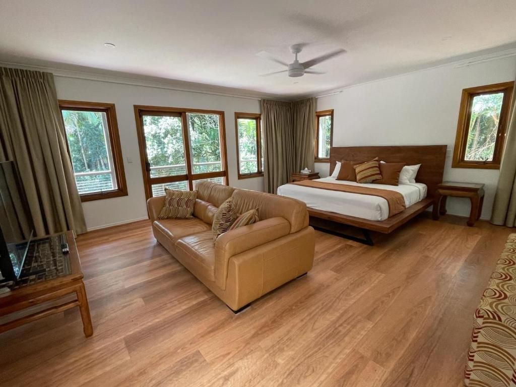 Quarto de hotel com cama, sofá, televisão e amplas janelas.