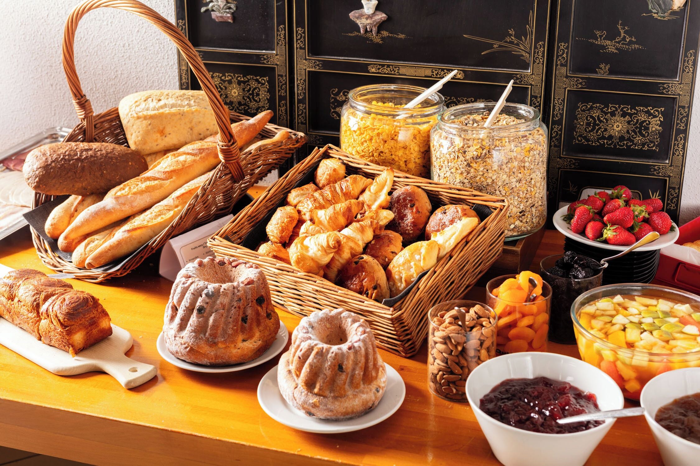 Diversos pães, doces e frutas sobre uma mesa.