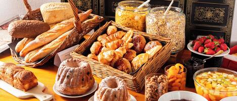 Diversos pães, doces e frutas sobre uma mesa.