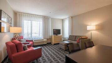 Quarto de hotel com sofá, poltrona, mesa de jantar, televisão e abajur.
