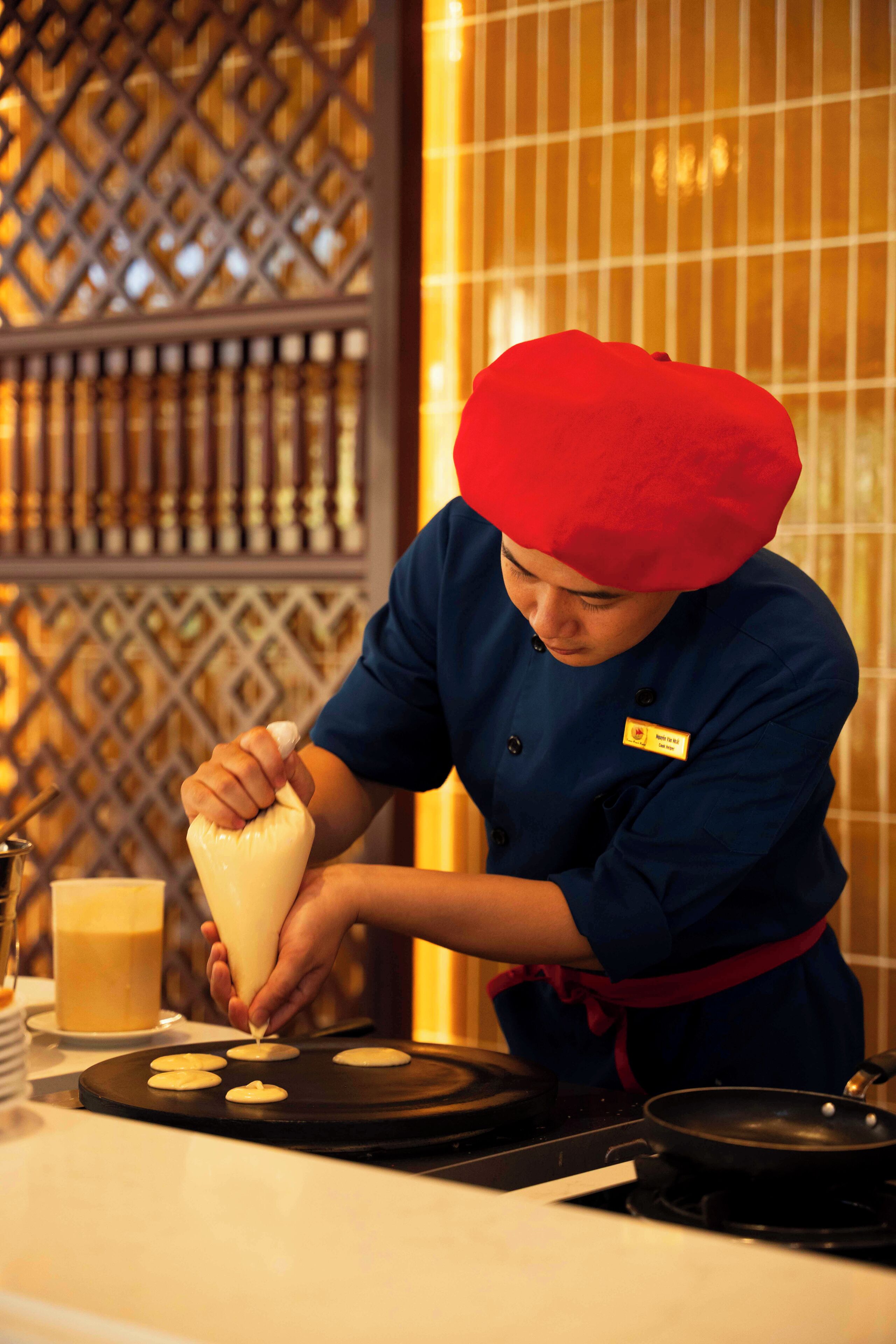 Um cozinheiro com uniforme azul e chapéu vermelho preparando comida em uma bancada de cozinha.