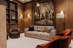 Uma sala de estar moderna com um sofá, poltronas, uma estante e um quadro grande na parede.
