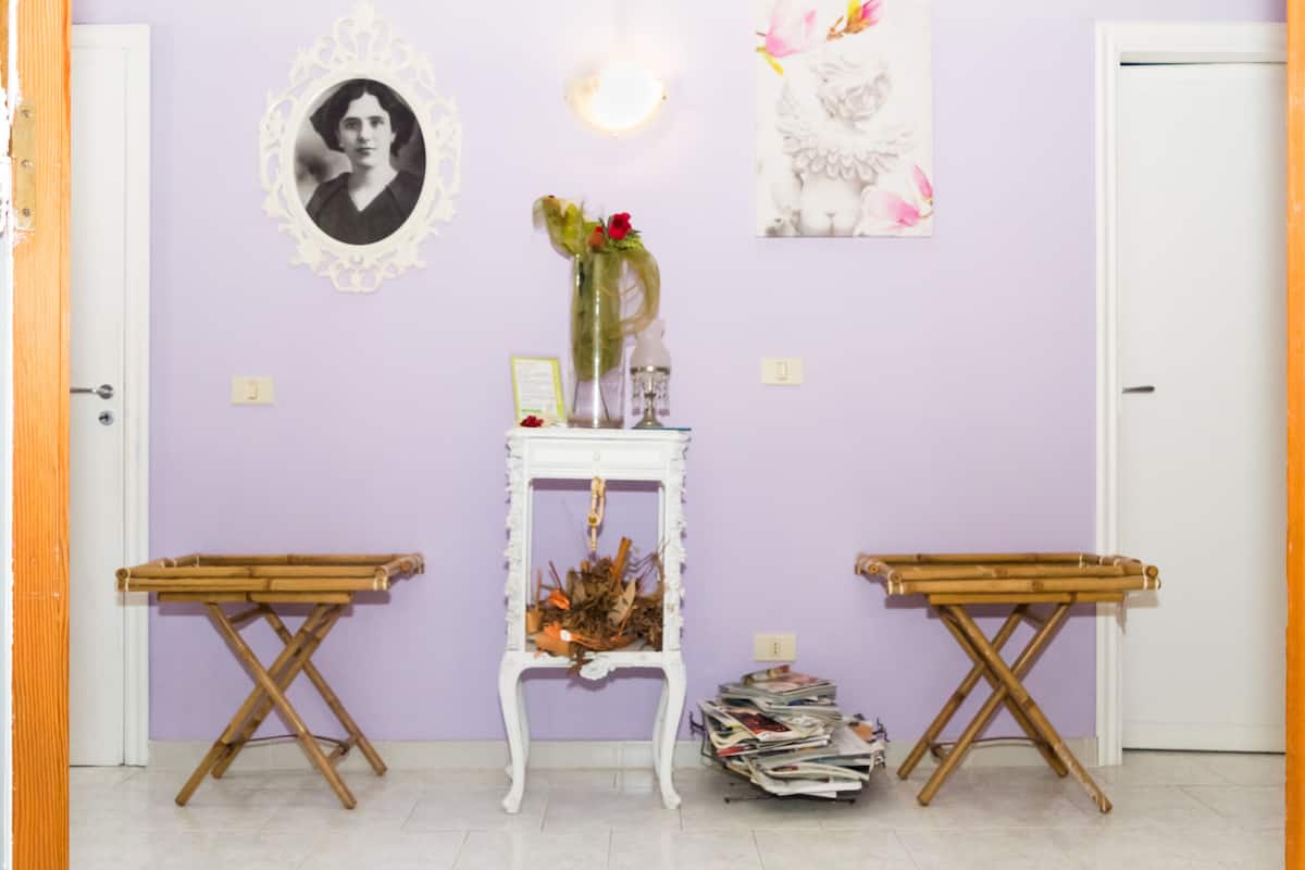 Quarto com parede roxa, porta branca e duas mesas dobráveis de madeira.