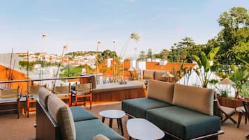 Terraço no telhado com área de estar ao ar livre, incluindo sofás e cadeiras, e vista para a paisagem urbana ao fundo.