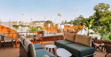Terraço no telhado com área de estar ao ar livre, incluindo sofás e cadeiras, e vista para a paisagem urbana ao fundo.