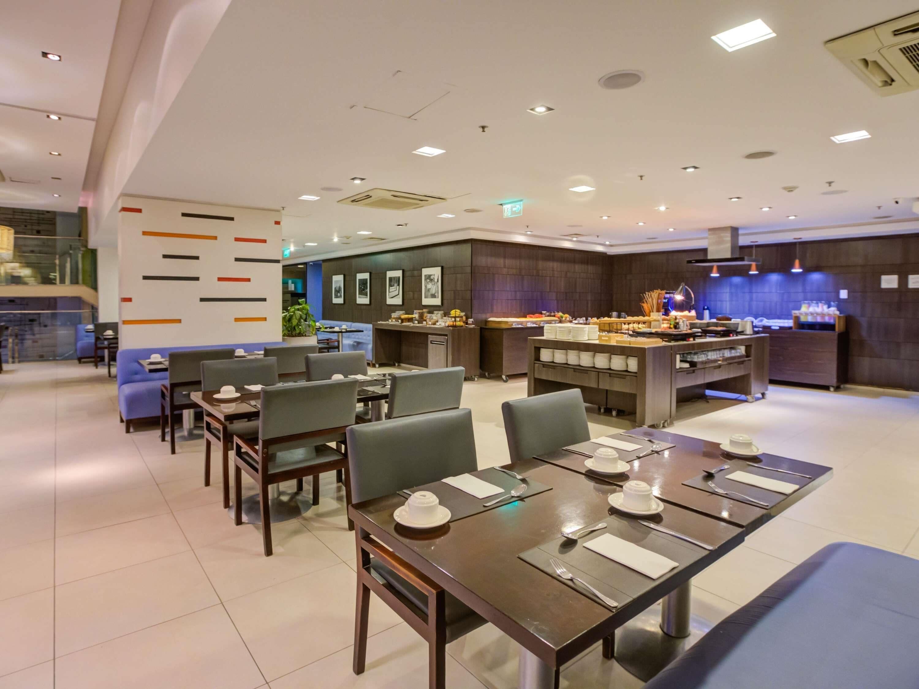 Restaurante moderno com espaço para buffet, assentos para hóspedes e balcão de atendimento.