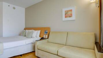 Quarto de hotel com cama, sofá, mesa de cabeceira, luminária e um quadro na parede.