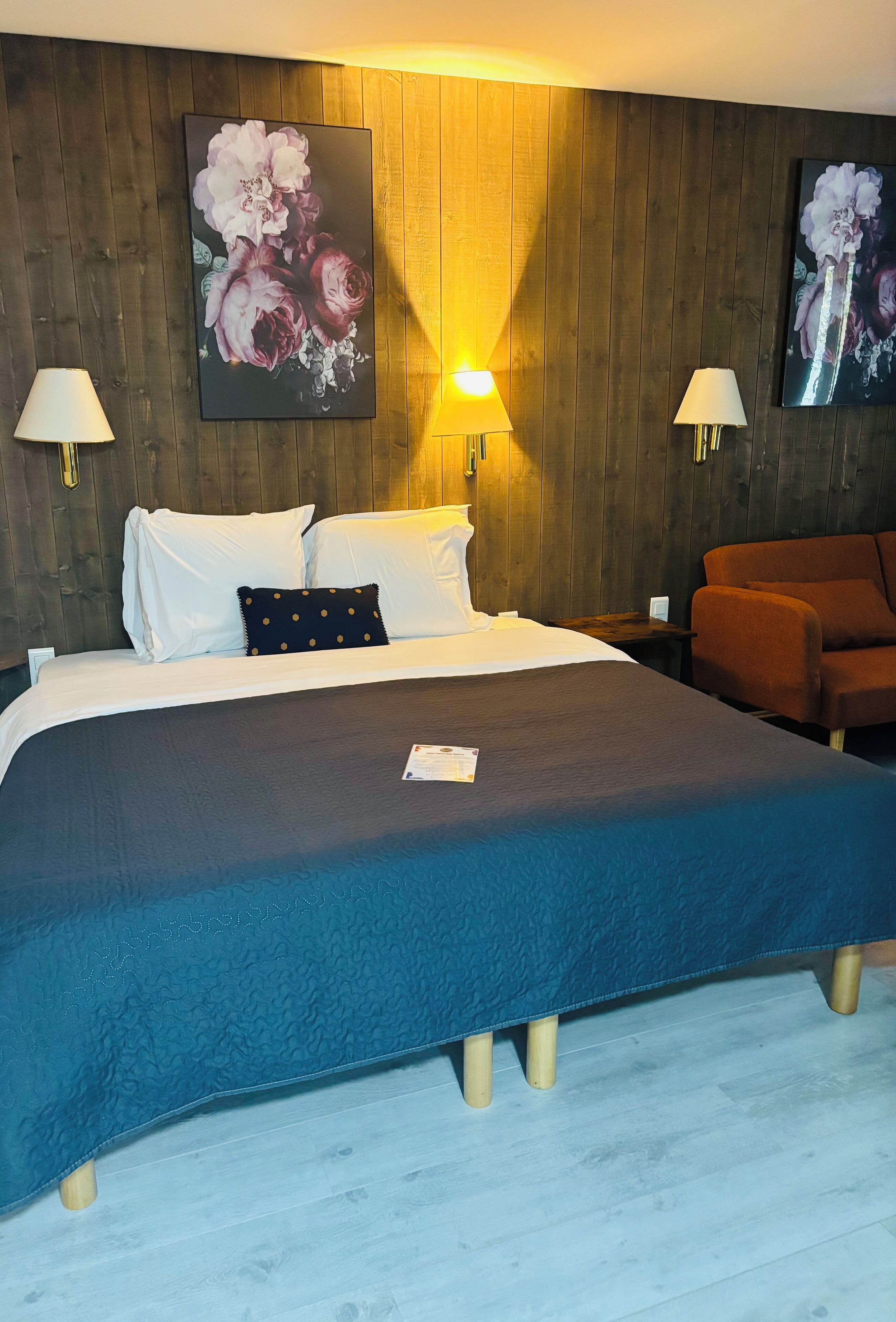 Quarto de hotel com uma cama grande, duas luminárias fixadas na parede e um painel de parede em madeira.