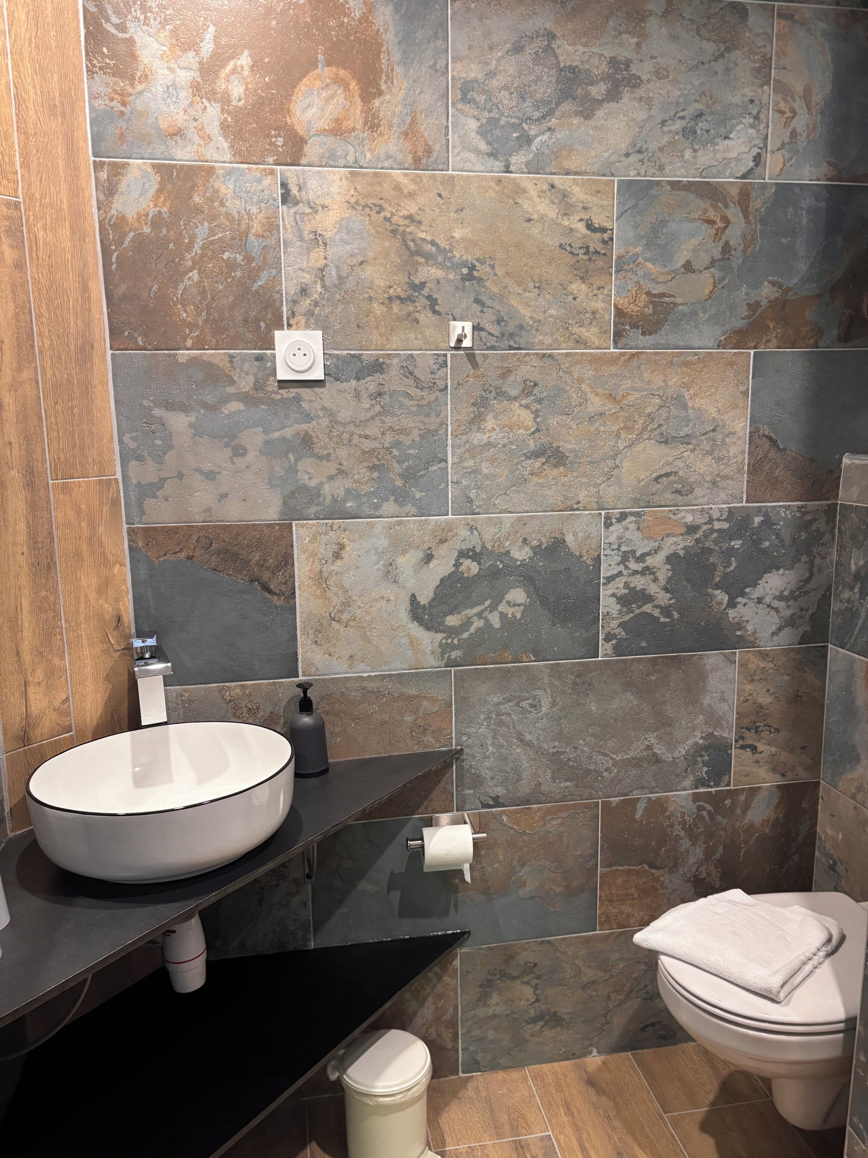 Casa de banho com lavatório branco, bancada preta e sanita.