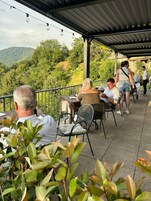 Pátio externo com mesas e cadeiras, com vista para uma paisagem montanhosa.