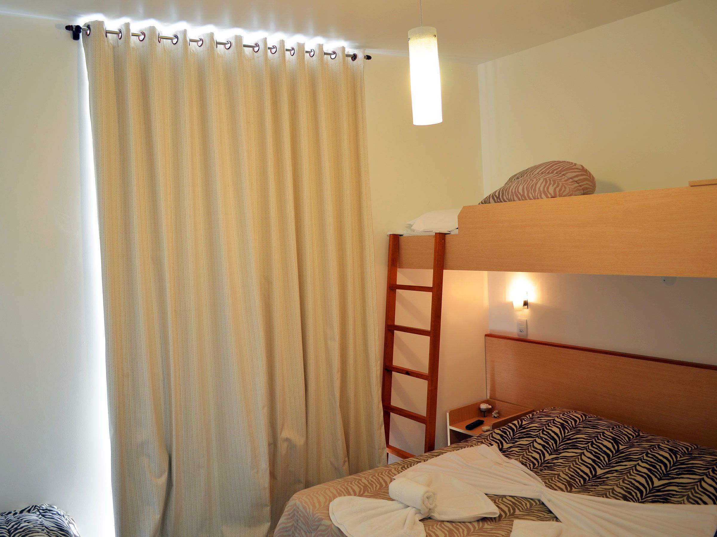 Uma cama beliche com travesseiro estampado com padrão de zebra, uma escada de madeira, uma mesa de cabeceira com controle remoto e uma cortina.