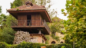 Uma casa de madeira com varanda, rodeada por vegetação exuberante e um muro de pedra.
