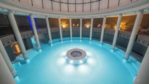 Uma piscina interior ampla com um elemento circular central, rodeada por colunas e áreas de estar.