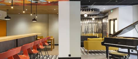 Um hall moderno com um piano, uma área de bar com cadeiras vermelhas e um chão xadrez.