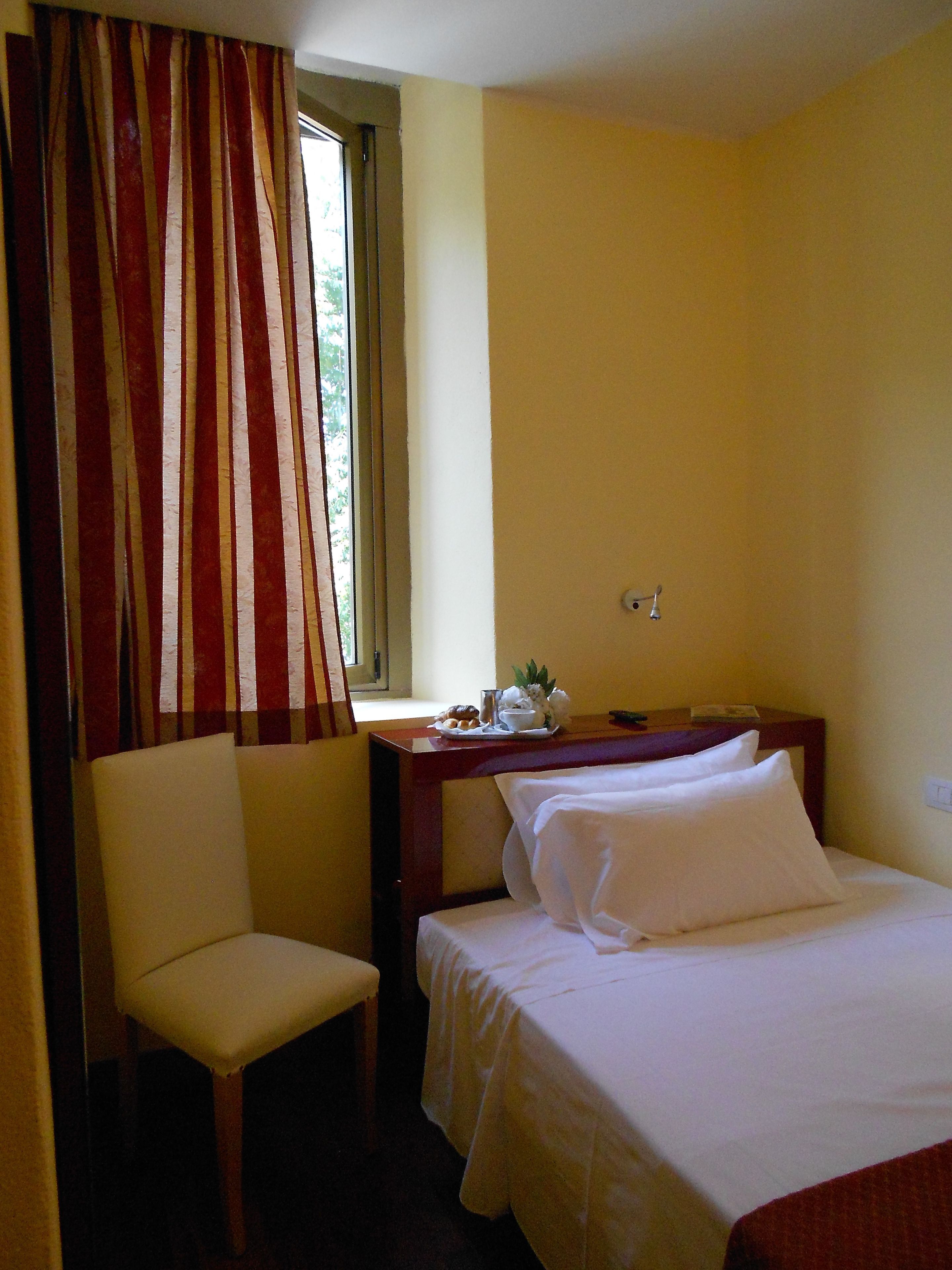 Quarto de hotel com cama, uma cadeira, uma mesinha com uma bandeja de itens de café da manhã e janela com cortinas.