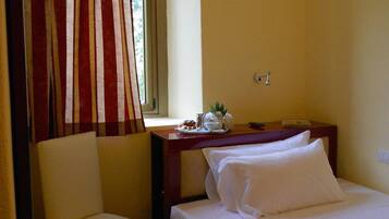 Quarto de hotel com cama, uma cadeira, uma mesinha com uma bandeja de itens de café da manhã e janela com cortinas.