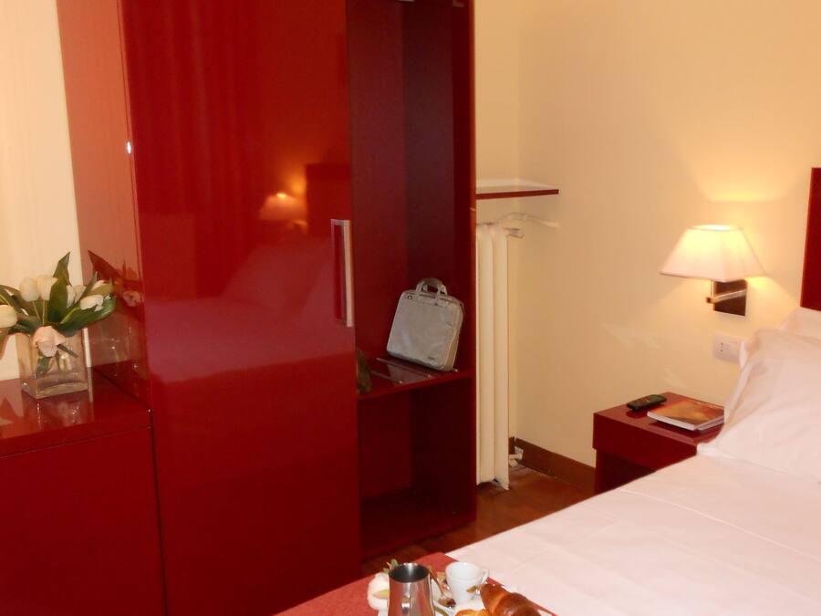 Quarto de hotel com cama, um guarda-roupa vermelho, mesa de cabeceira com abajur e bandeja com itens de café da manhã.