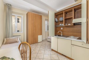 Quarto compacto com cama, guarda-roupa de madeira, cozinha compacta com pia e janela com cortinas.