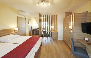 Quarto de hotel com cama, escrivaninha, cadeira, televisão e uma mesinha de apoio com controle remoto.