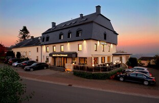 Um hotel com restaurante, vários carros estacionados e um céu ao pôr do sol.