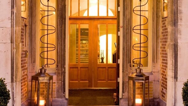Entrada de edifício com o número '36' grande acima da porta, duas luminárias laterais e fachada de tijolos.