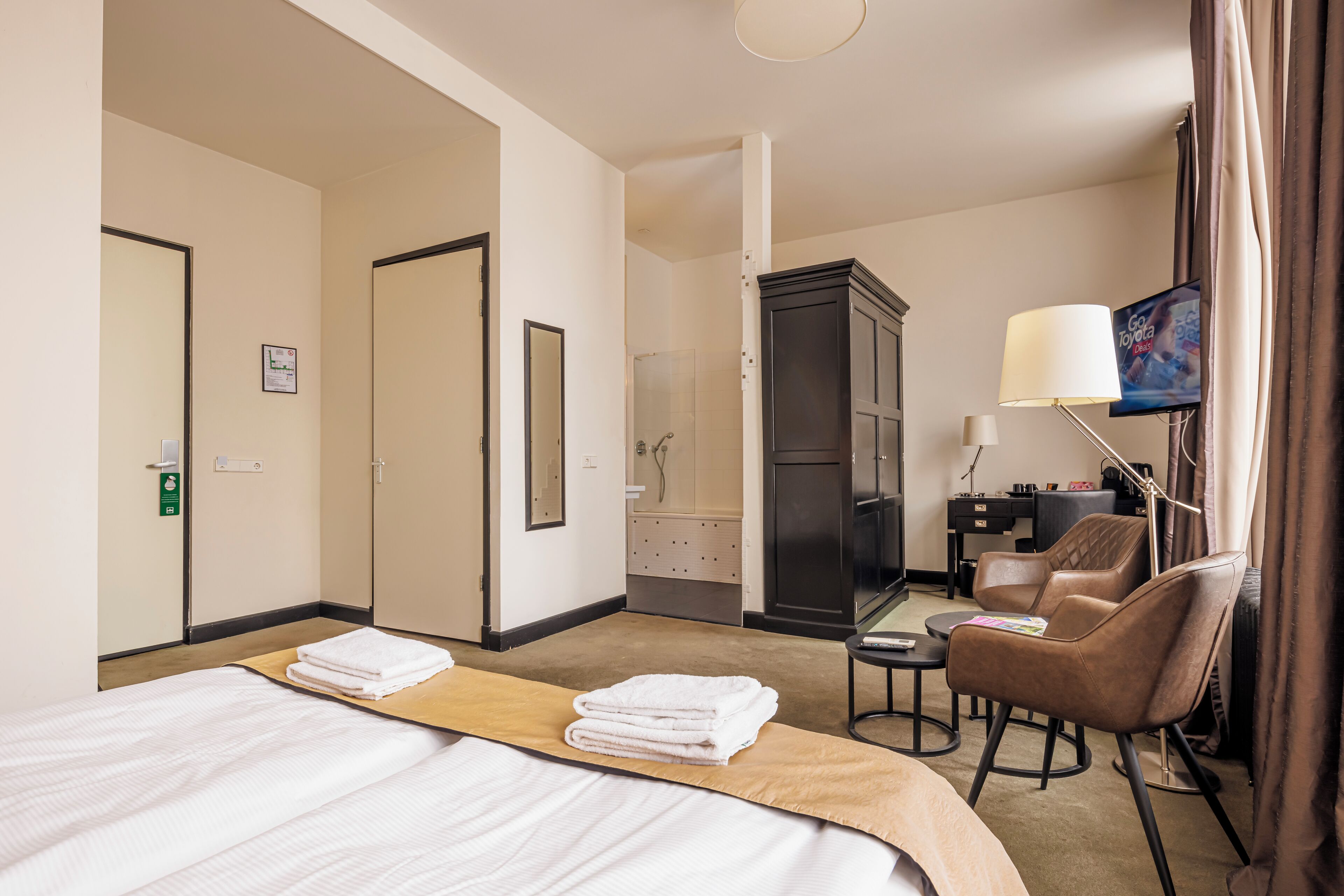 Quarto de hotel com cama, escrivaninha, cadeira, televisão e banheiro.
