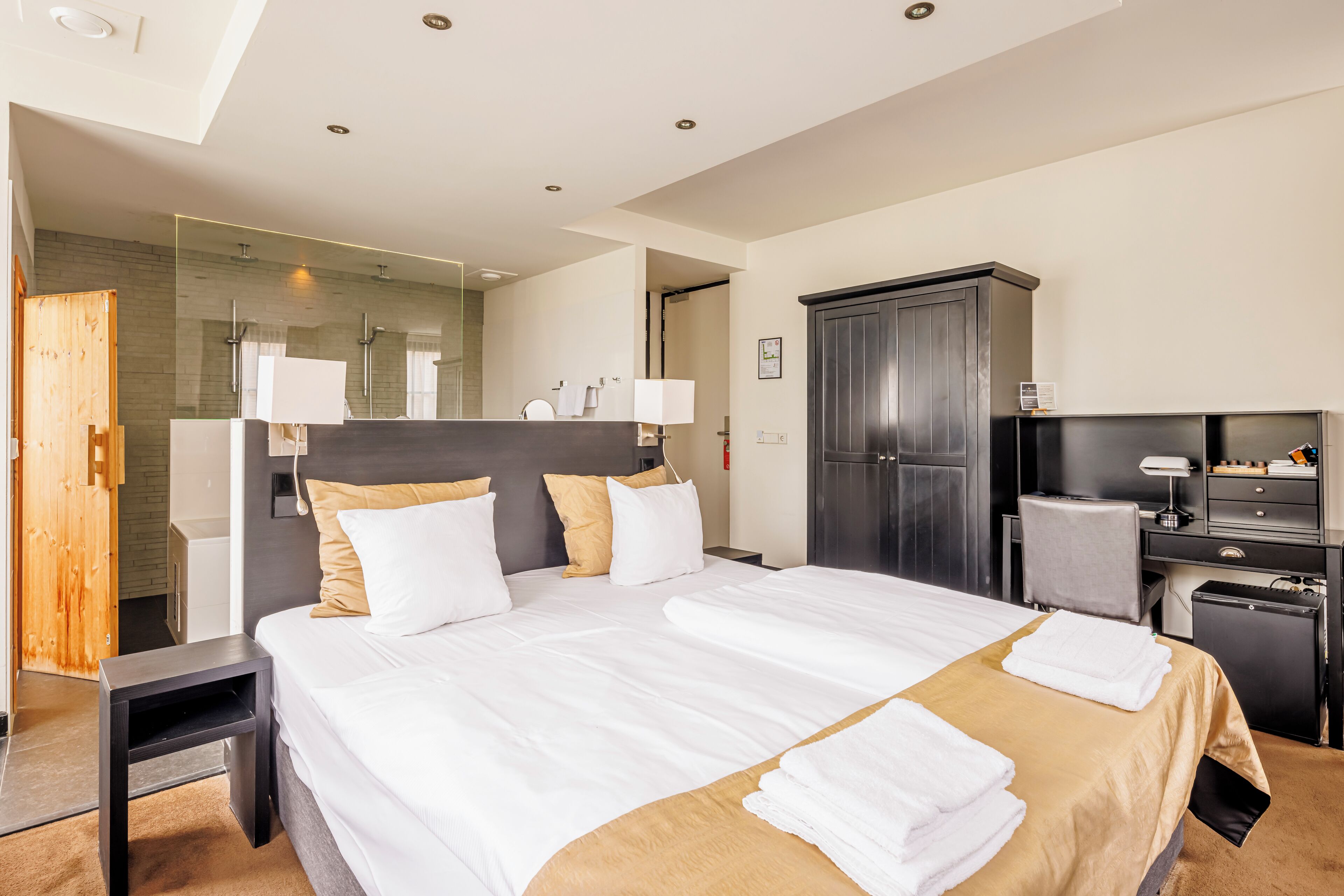 Quarto de hotel com uma cama grande, uma escrivaninha, um guarda-roupa e um banheiro visível por uma porta aberta.