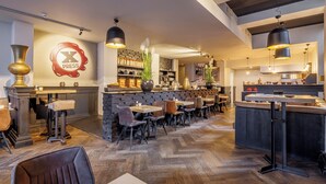 Interior de restaurante moderno com piso de madeira em padrão herringbone, mobiliário preto e de madeira, e iluminação pendente.