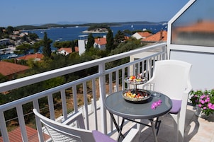 Varanda com mesa e cadeiras, com vista para a costa, incluindo barcos e edifícios.