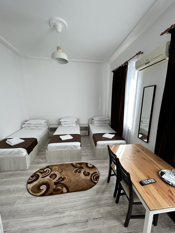 Quarto de hotel com quatro camas individuais, uma mesa de jantar de madeira, um espelho e um ventilador de teto.
