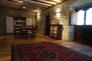 Quarto rústico com mesa de jantar de madeira, cadeiras, tapete vermelho estampado, paredes de pedra e um armário de madeira com portas de vidro.