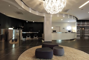 Um lobby moderno com balcão de recepção curvo, área de bar e assentos com pufes.