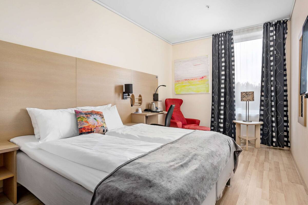 Quarto de hotel com uma cama grande, uma mesa, uma cadeira e uma televisão.