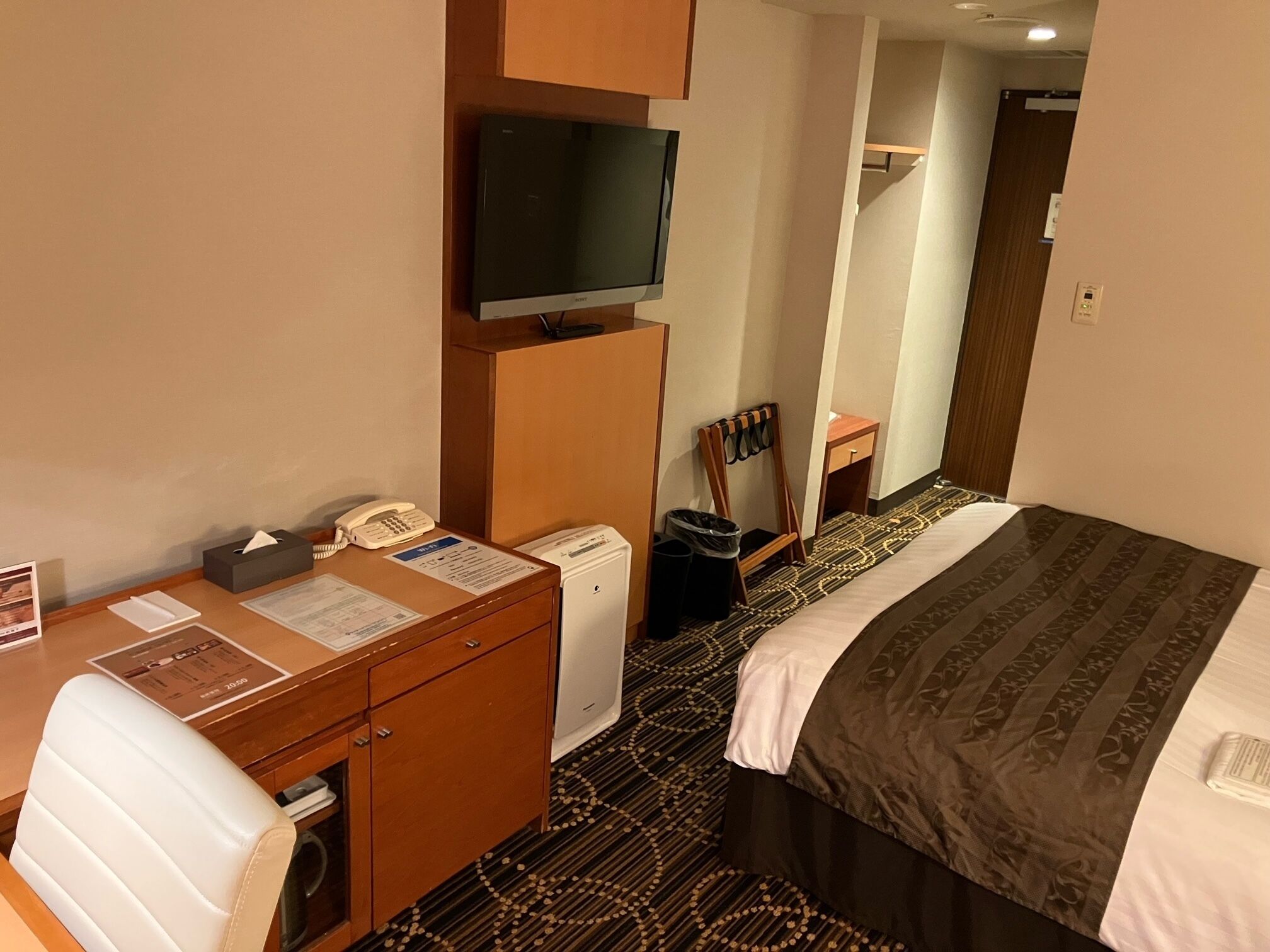 Quarto de hotel com escrivaninha, telefone, televisão, cama e espelho.