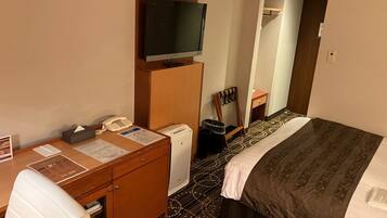 Quarto de hotel com escrivaninha, telefone, televisão, cama e espelho.
