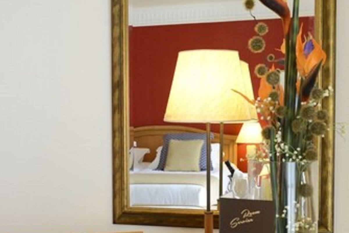 Quarto de hotel com uma mesa de jantar posta para dois, um espelho, um abajur e um vaso com flores.
