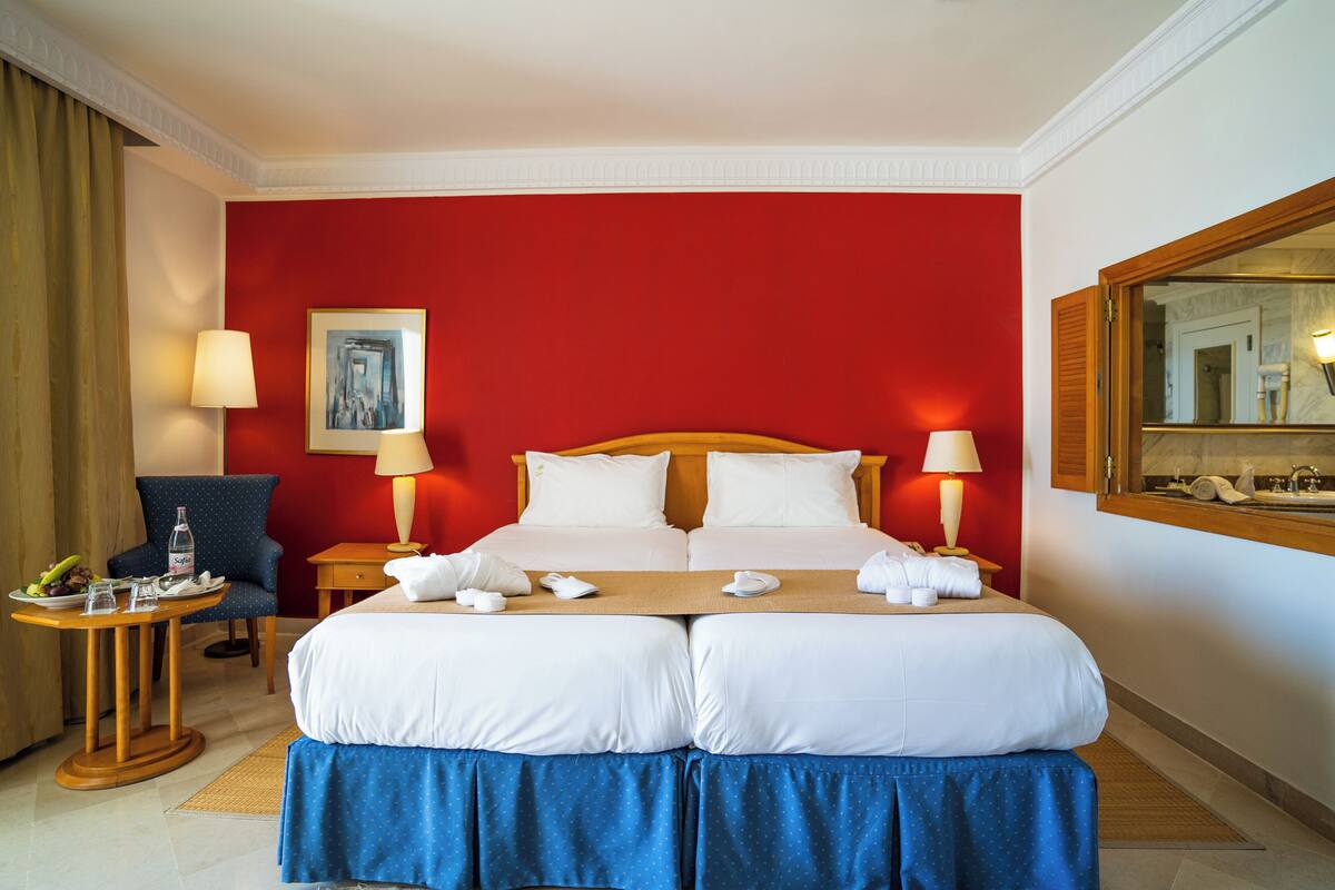 Uma cama de casal com roupa de cama branca, uma cabeceira de madeira e duas mesas de cabeceira com abajures.