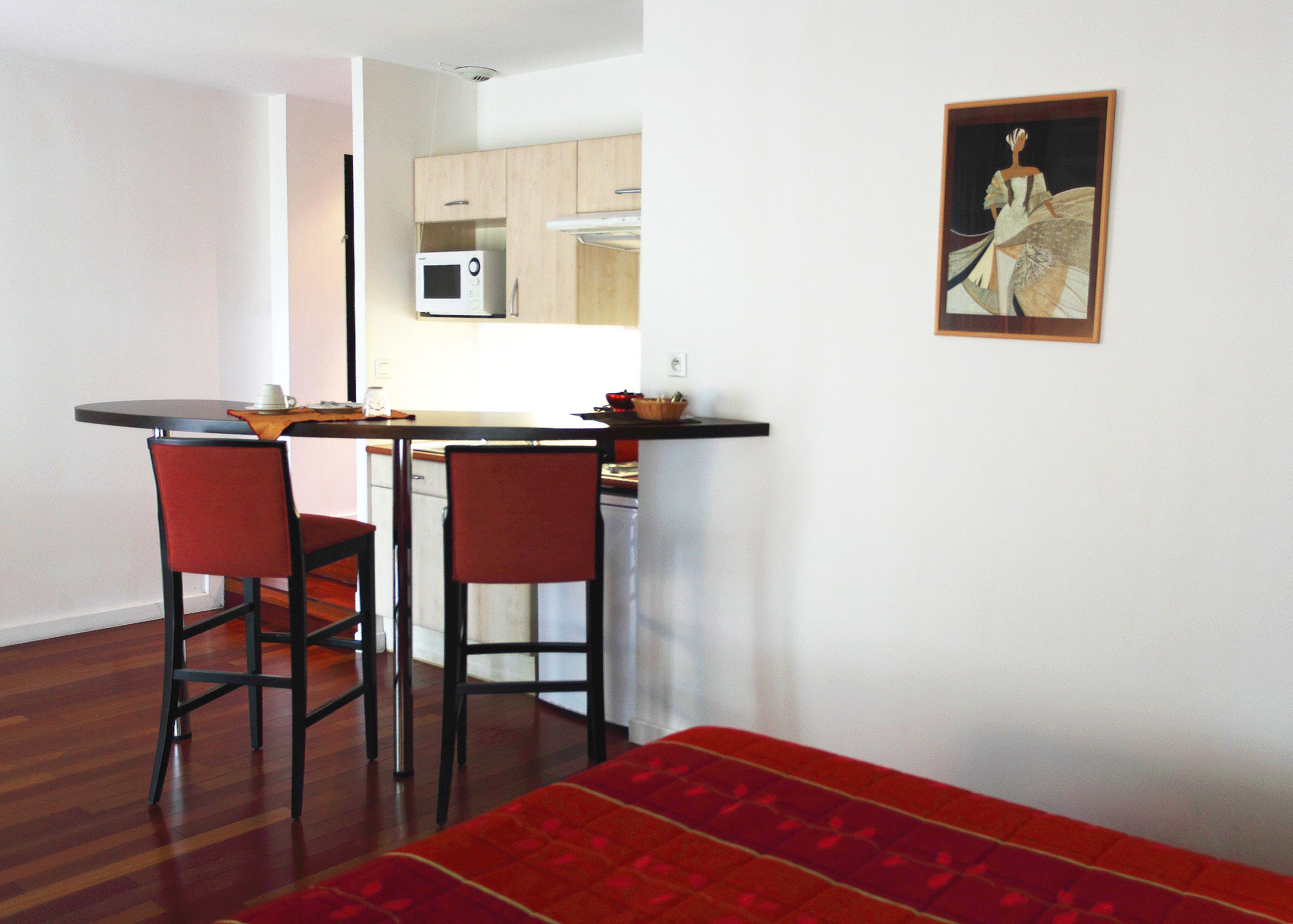 Um espaço de estar compacto com cozinha compacta, dois banquetas, uma mesa de jantar e um tapete estampado em vermelho.