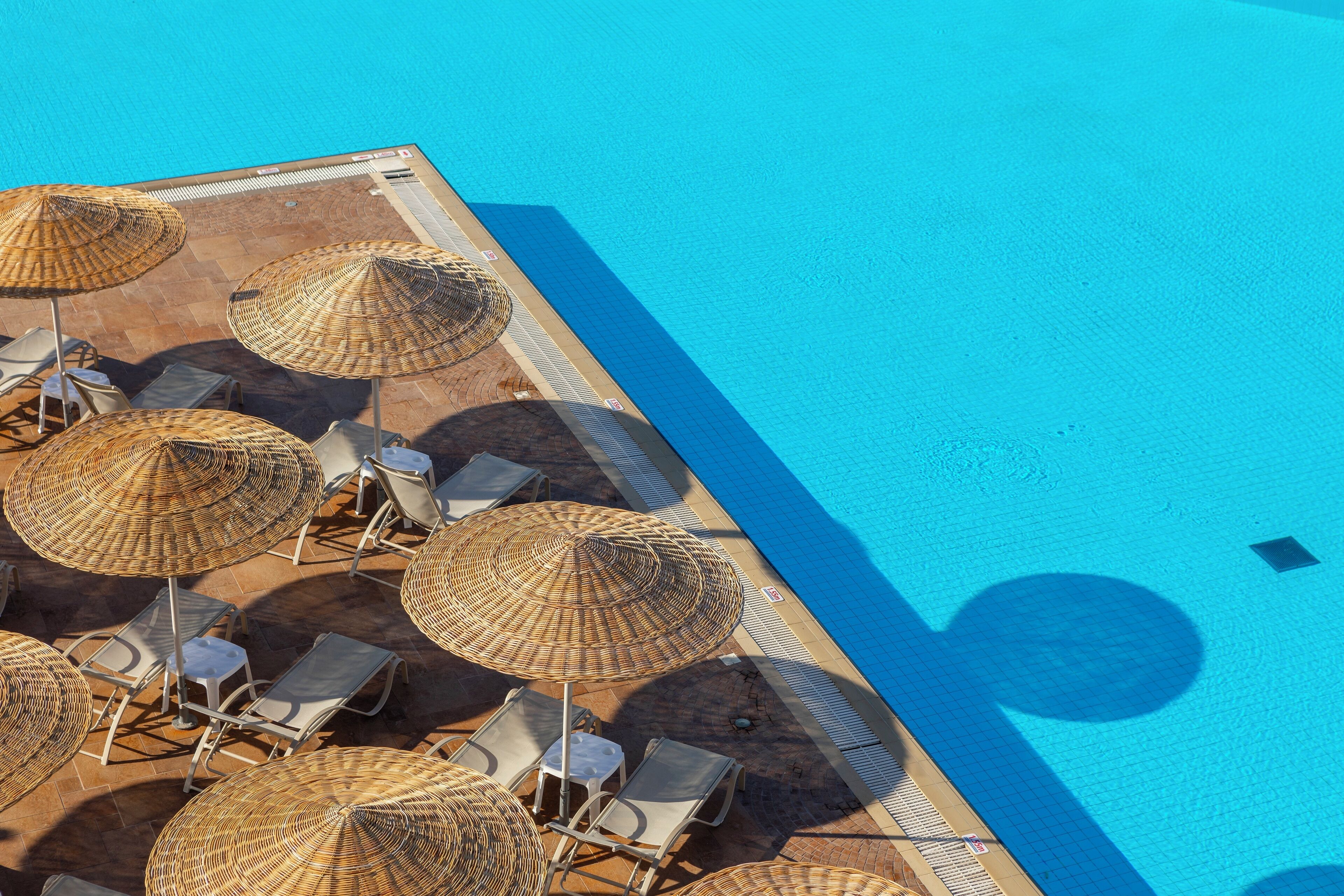 Uma área à beira da piscina com espreguiçadeiras e guarda-sóis de tecido.