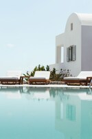 Uma área à beira da piscina com espreguiçadeiras e um edifício branco com telhado curvo.