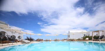 Área ao redor da piscina com espreguiçadeiras e guarda-sóis, céu limpo e uma piscina.