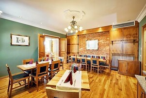 Uma sala de jantar com mesas e cadeiras de madeira, parede de tijolos e um candelabro.