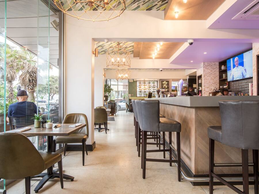 Uma área de bar moderna com balcão, banquetas e uma tela de televisão.