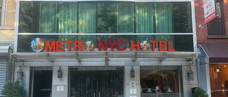 Exterior do Hotel Metro NYC, com entrada desobstruída, sinalização em vários idiomas e placa indicando que não é permitido estacionar.