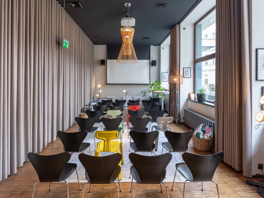 Uma sala de conferências moderna com fileiras de cadeiras pretas e amarelas, uma tela grande e piso de madeira.