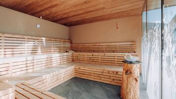 Uma sauna com bancos de madeira e piso de pedra, uma mesa de madeira com uma tigela, e uma parede de vidro com vista.