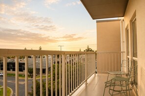Uma varanda com vista para uma estrada e edifícios, cadeiras de metal e um edifício com fachada bege.