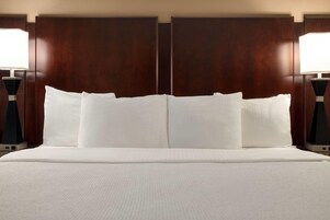Uma cama grande com lençóis brancos e cabeceira de madeira.