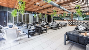 Uma área externa moderna com assentos em sofás estampados em preto e branco, plantas penduradas e um bar ao fundo.