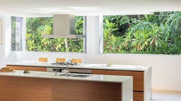 Cozinha moderna com ilha central, pia dupla e vista para vegetação exuberante através de amplas janelas.